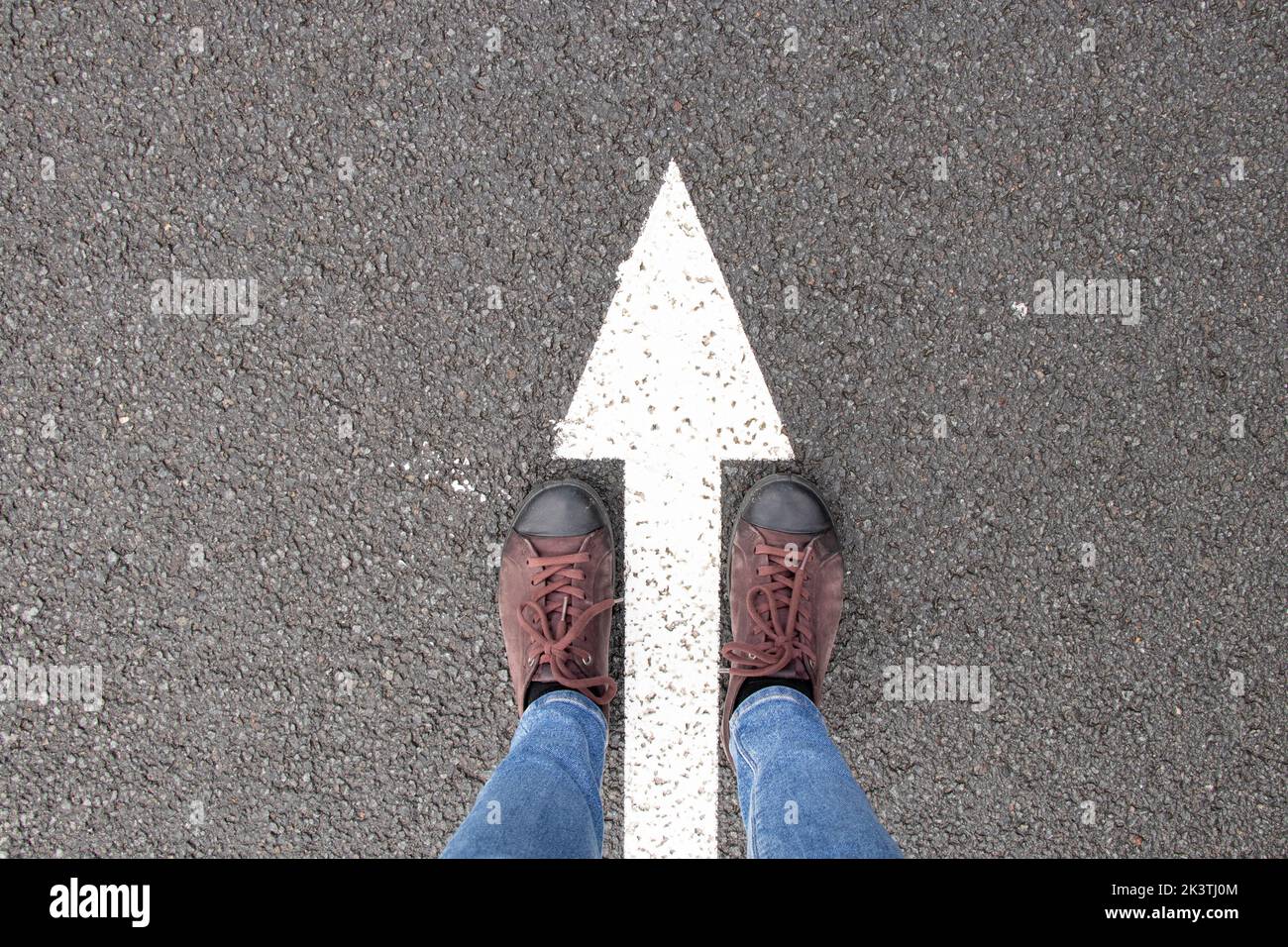 Women's feet stand on the forward arrows on the road, sneakers on the ...