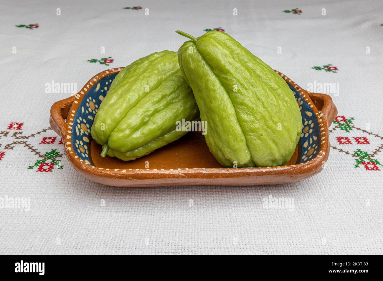 Two organically grown chayotes in a Mexican clay tray on a tablecloth ...