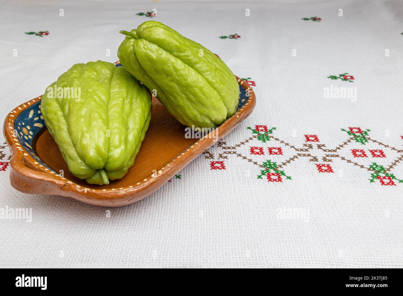 Two chayotes in a Mexican clay tray on a tablecloth with red cross ...