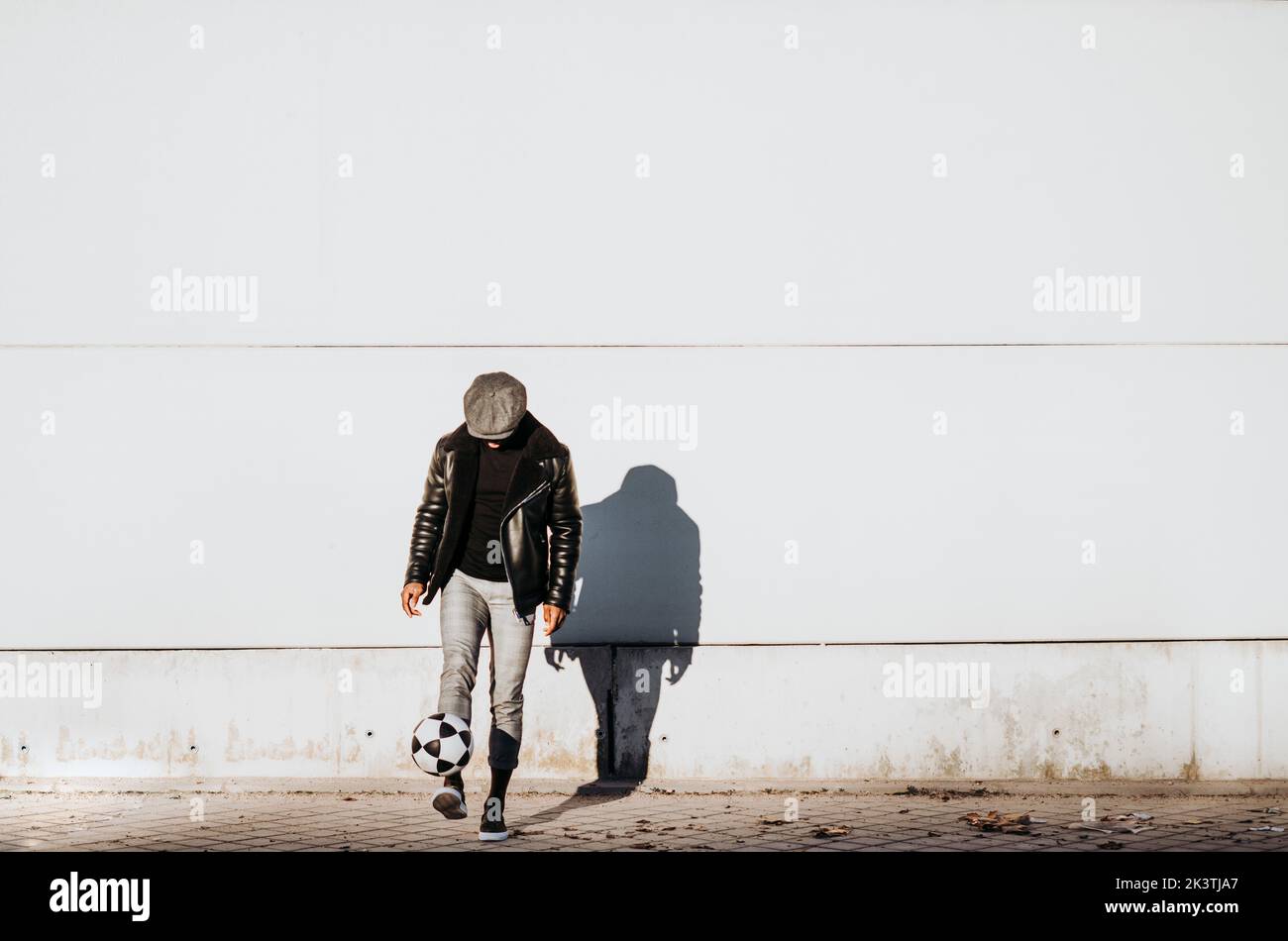 Black man kicking ball on street on white wall Stock Photo - Alamy