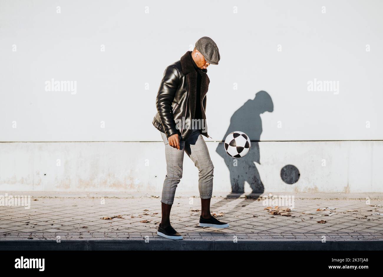 Black man kicking ball on street on white wall Stock Photo - Alamy