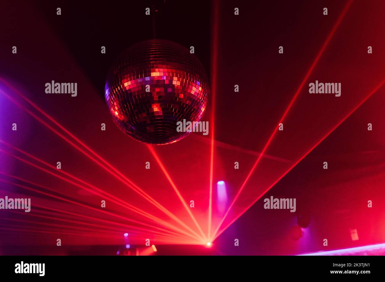 Modern disco ball shining under red neon light on ceiling of nightclub ...