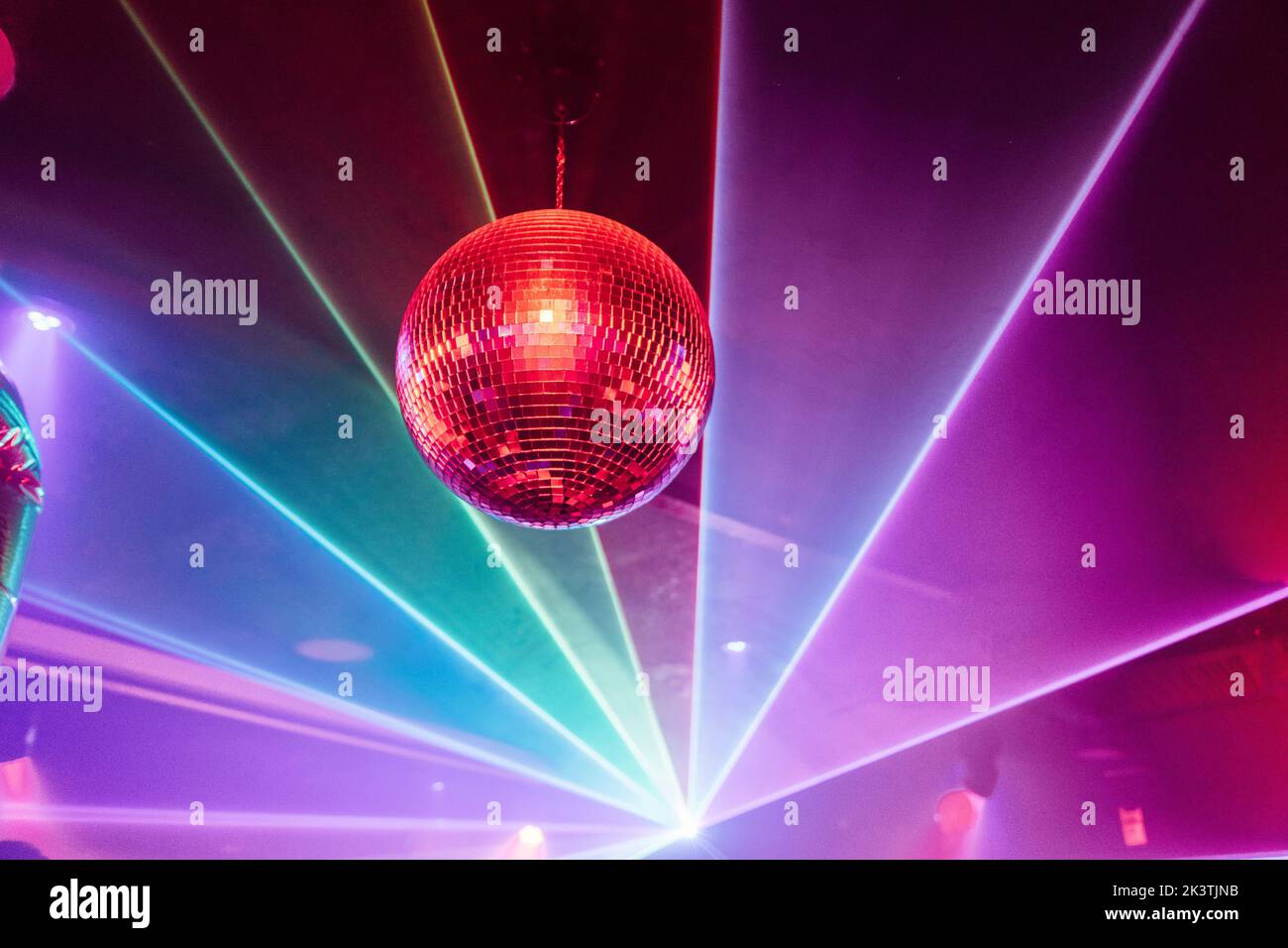 Modern disco ball shining under red neon light on ceiling of nightclub ...