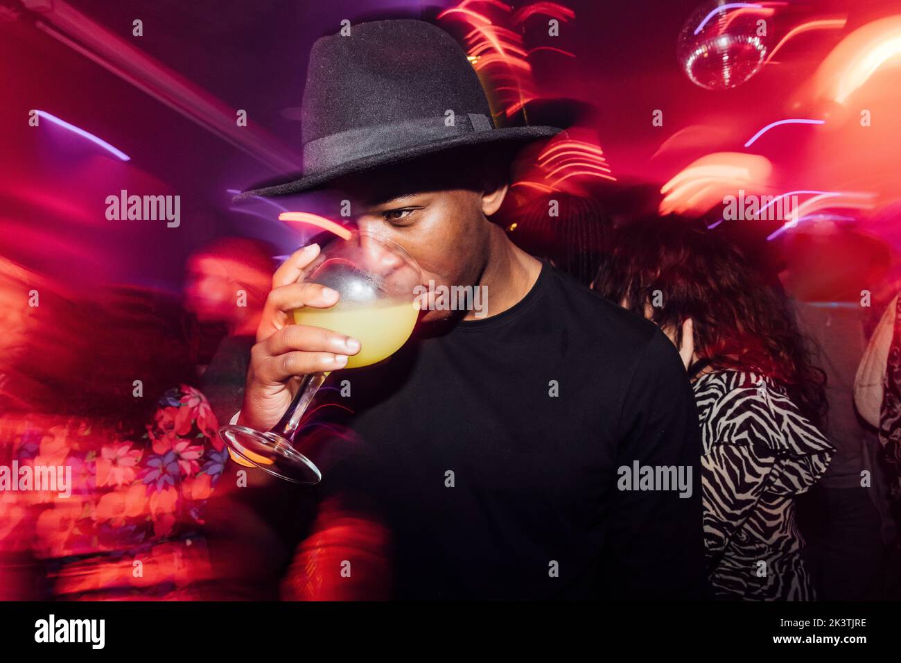 Low angle of African American guy sipping alcohol cocktail under ...