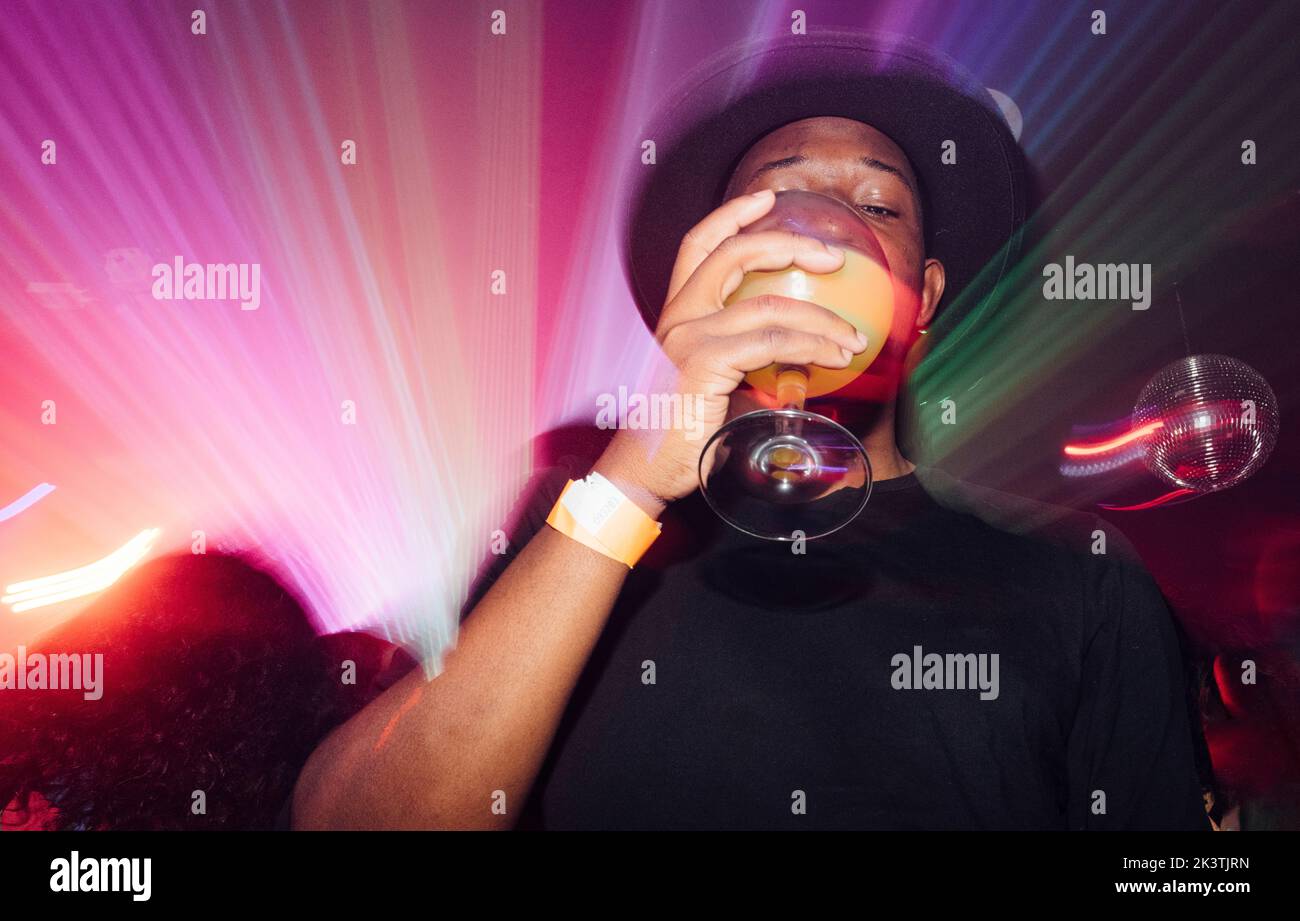 Low angle of African American guy sipping alcohol cocktail under ...