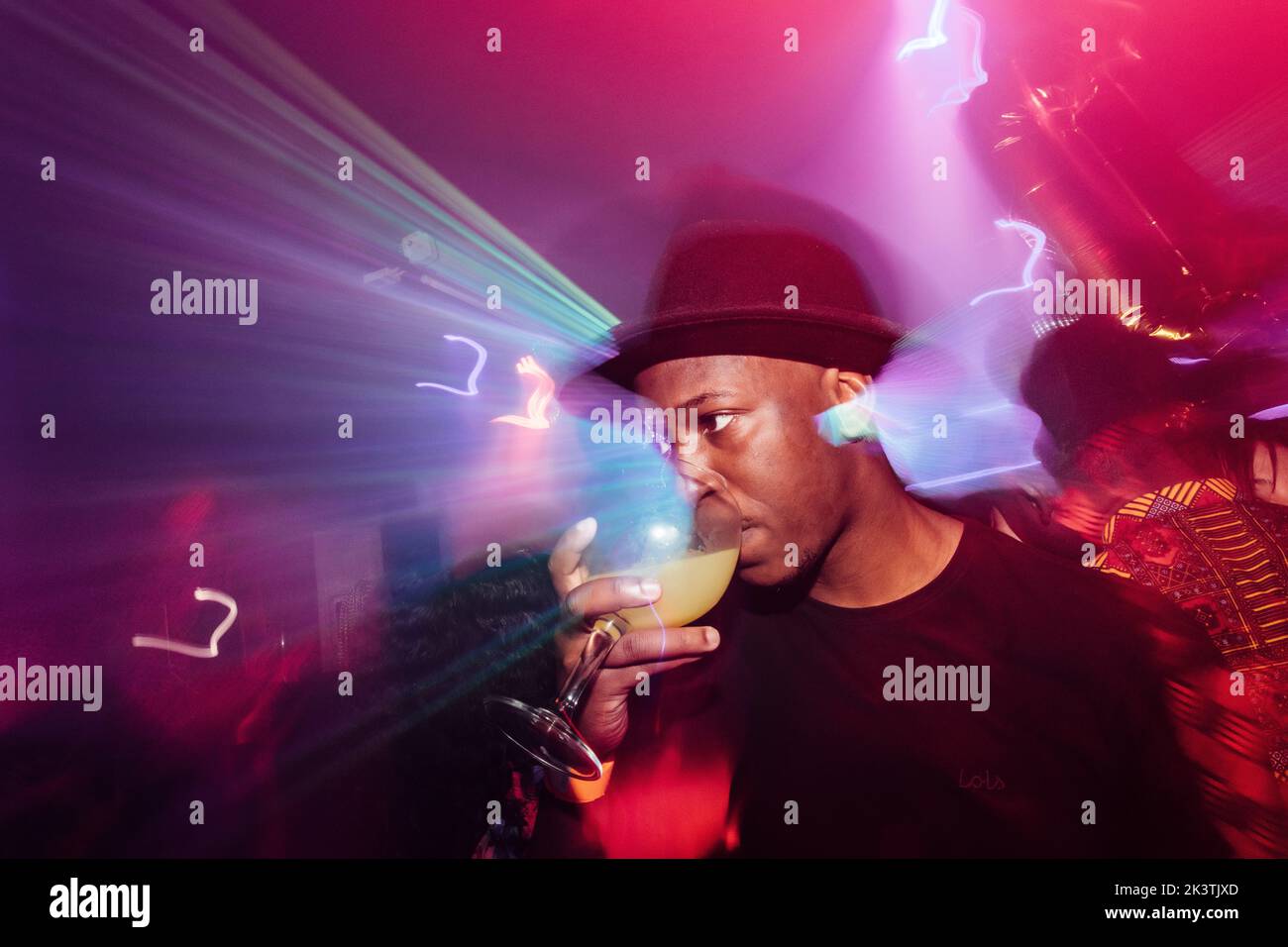 Low angle of African American guy sipping alcohol cocktail under ...