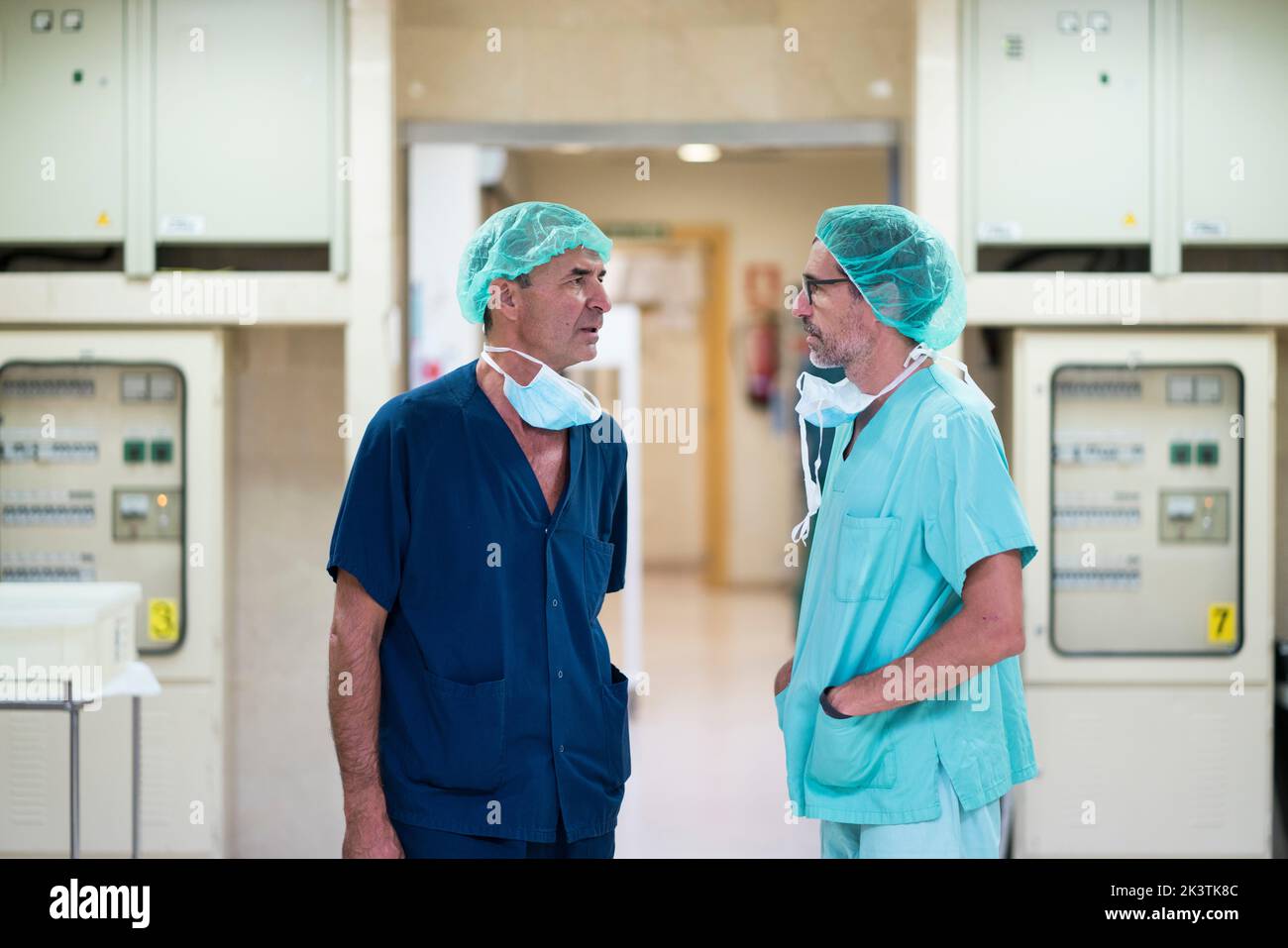 Side view of two men in scrubs speaking with each other while standing ...