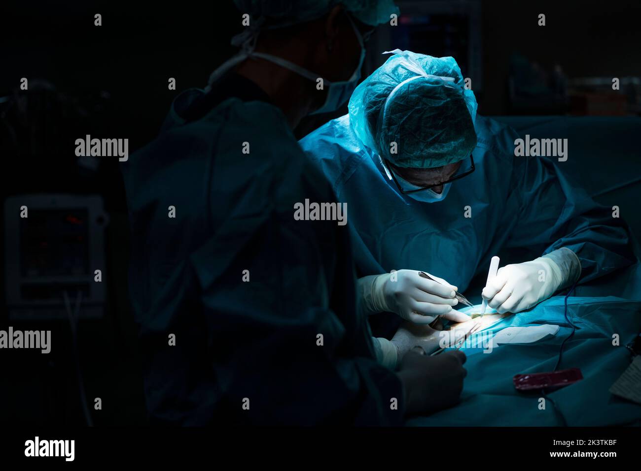 Two men in surgeon uniform conducting surgery on patient in dark ...