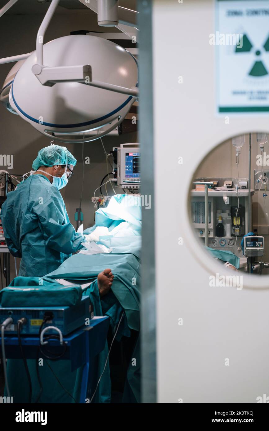 Side view of man in surgeon uniform standing near bed with patient in ...