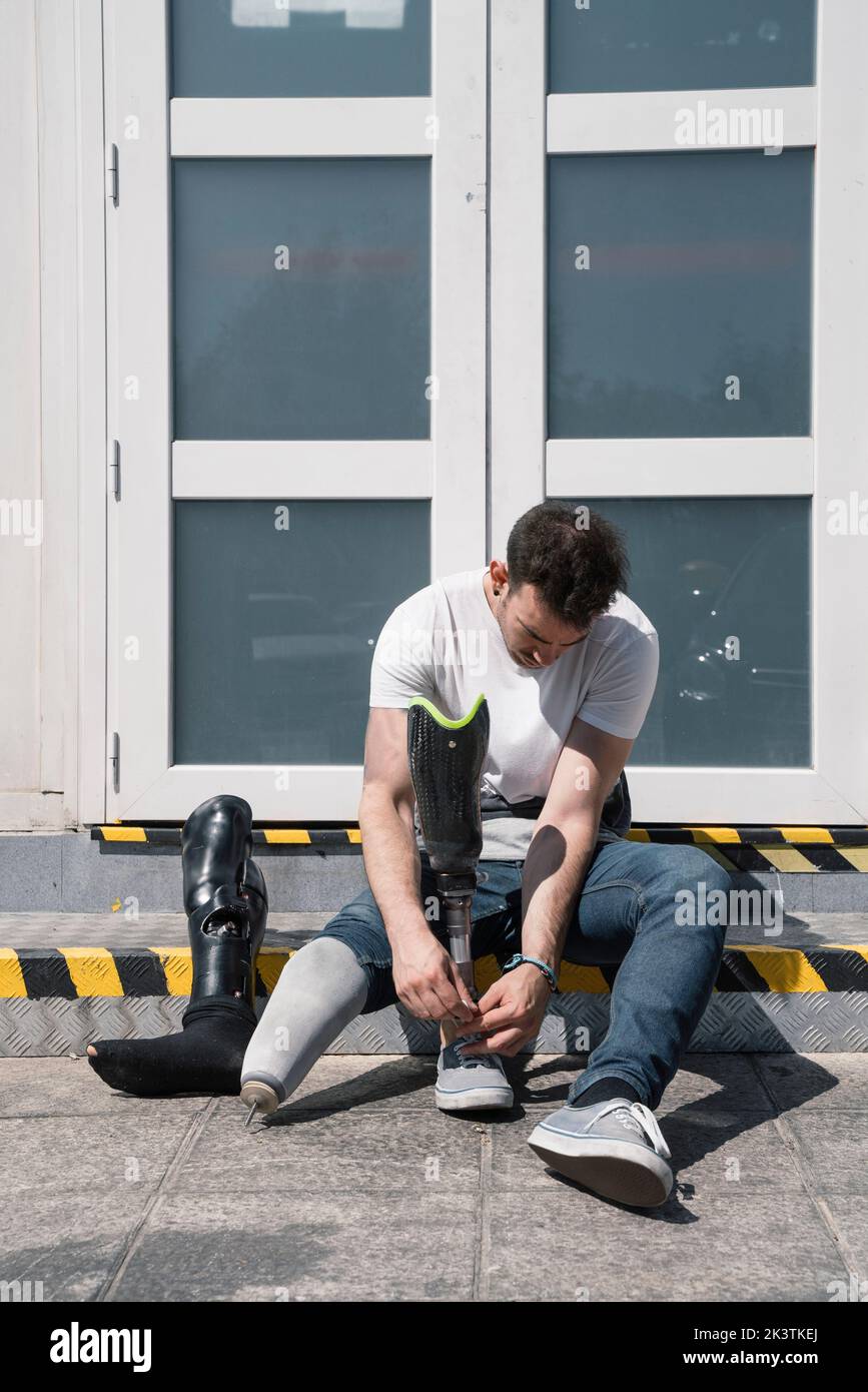 Young guy sitting on step and changing artificial leg while spending ...