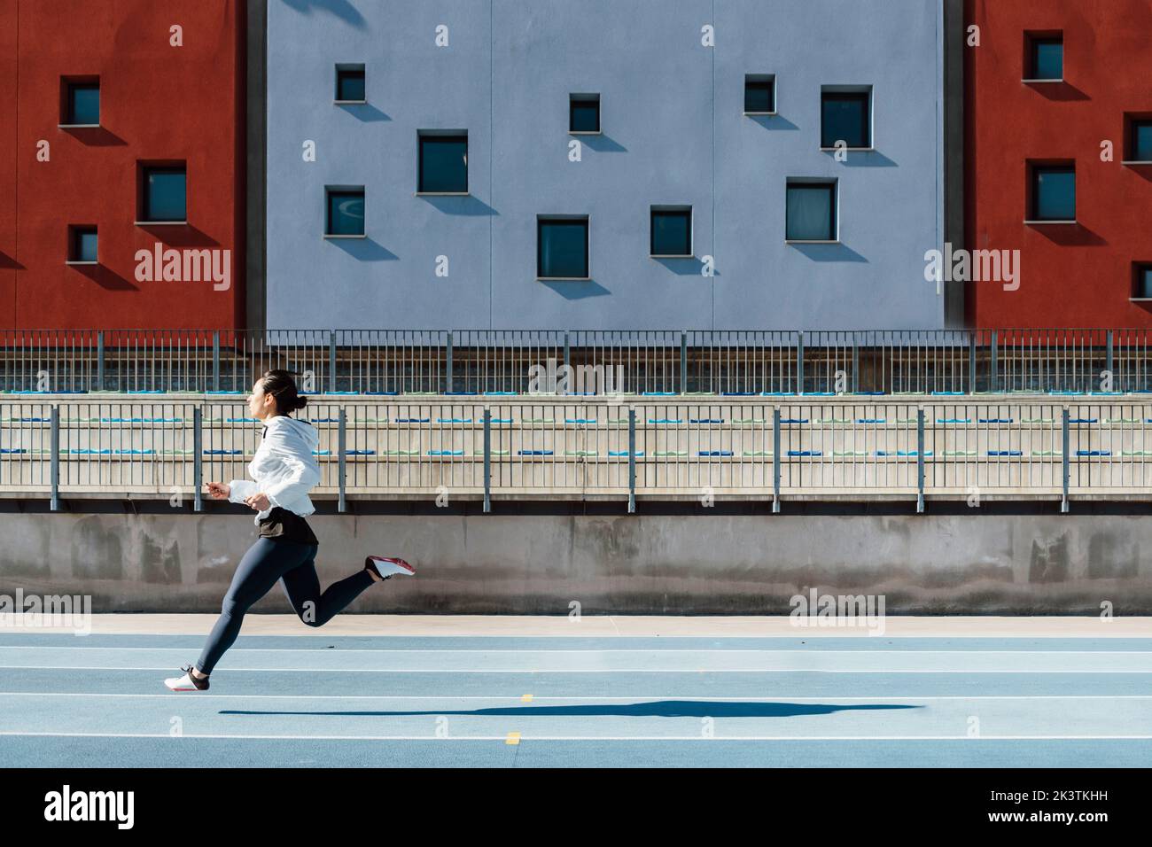 Side view of strong sportswoman running on blue racetrack fast during ...