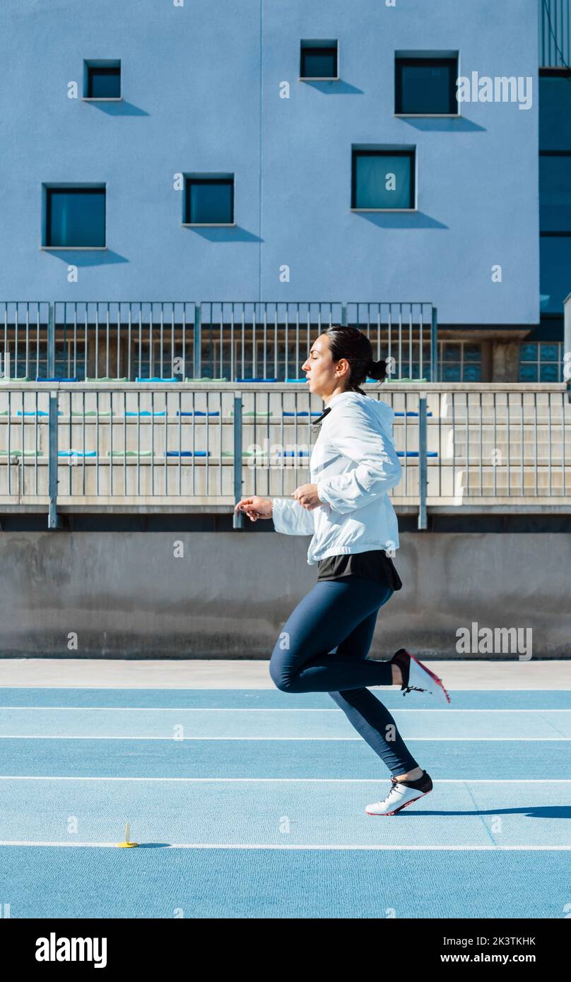 Side view of strong sportswoman running on blue racetrack fast during ...