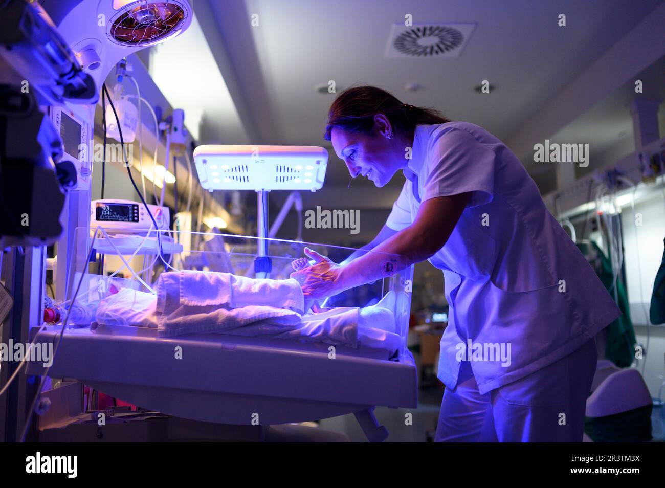 From above woman nurse holding small foot of sick tiny baby lying in ...