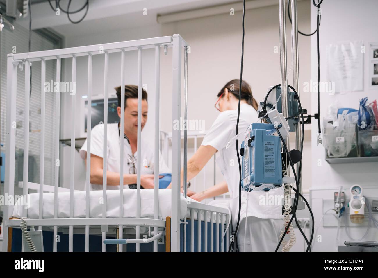 Doctors standing near hospital bed with newborn in intensive care unit ...