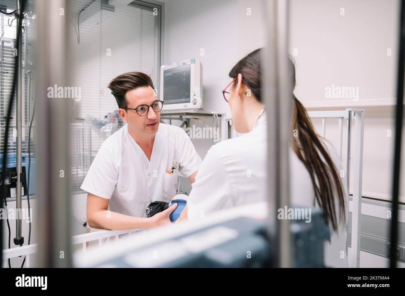 Doctors standing near hospital bed with newborn in intensive care unit ...
