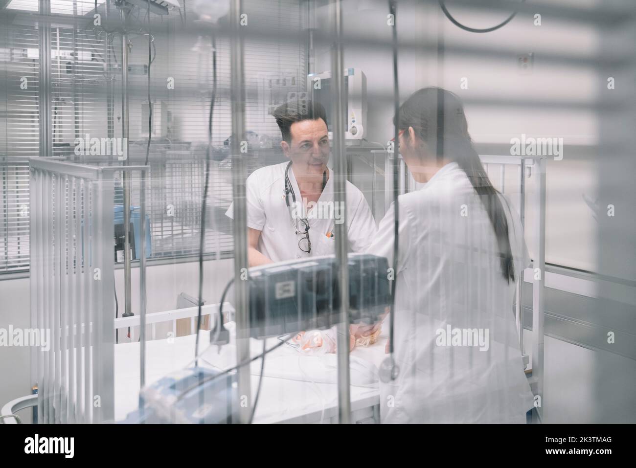 Doctors standing near hospital bed with newborn in intensive care unit ...