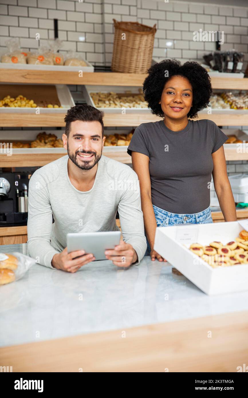 Bakery coworkers standing behind counter while holding digital tablet ...
