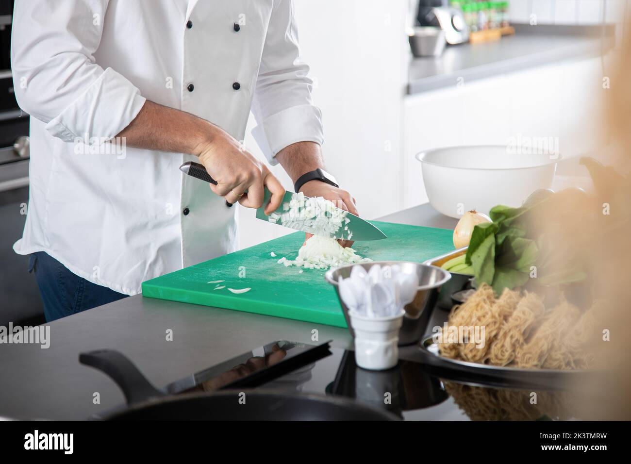 Crop man in white chef jacket using knife for cutting onion while ...