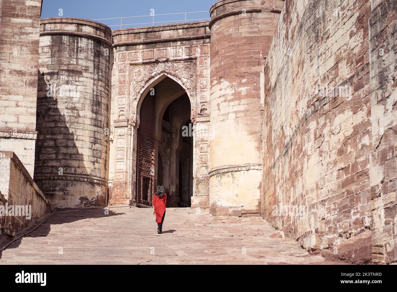 Back view of anonymous female walking on shabby path towards old gate ...