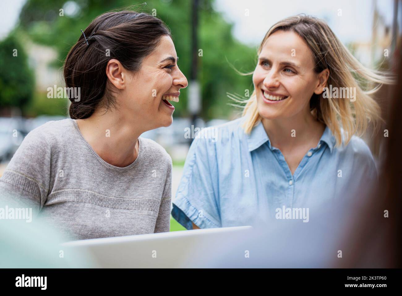 Female coworkers laughing while sitting outdoors Stock Photo - Alamy