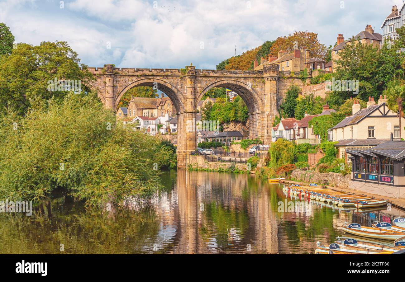 A historic stone viaduct straddles a river. Trees are on the bank and ...