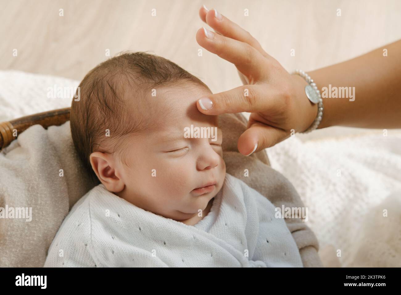 Crop woman with bracelet touching forehead of newborn baby sleeping in ...