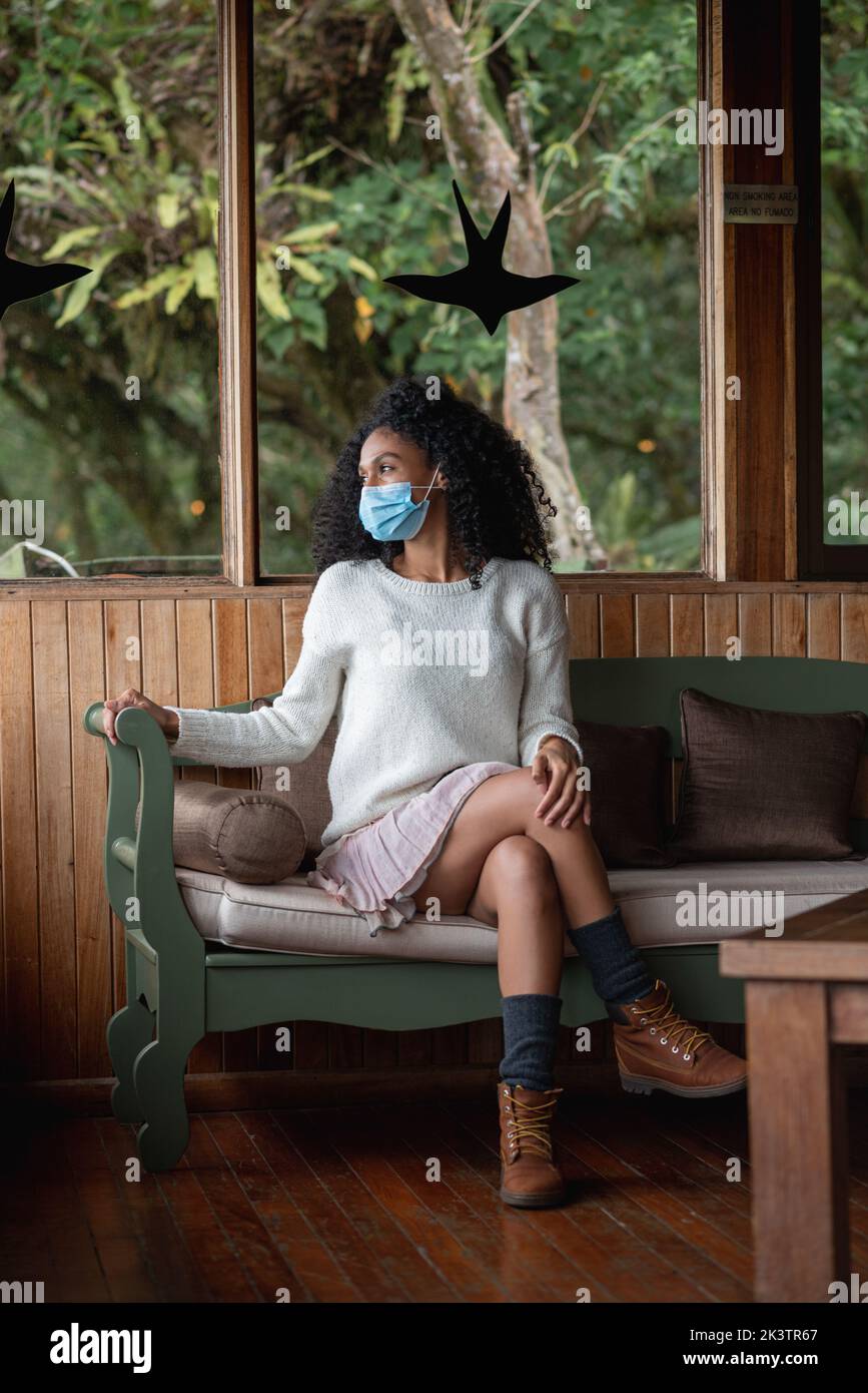 African American female in disposable mask sitting with crossed legs on ...