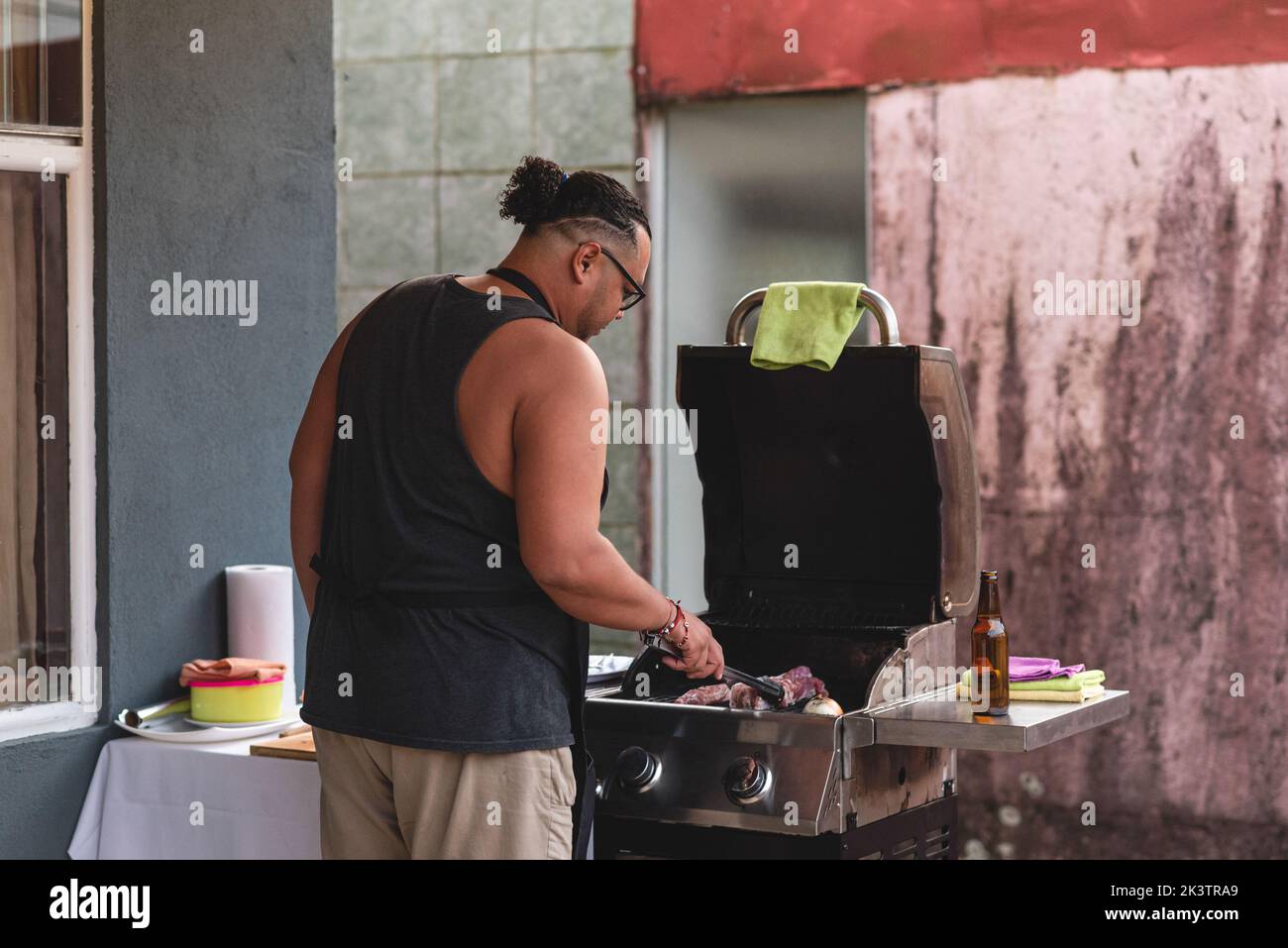 Back view of ethnic male in apron placing raw marinated meat on grill ...