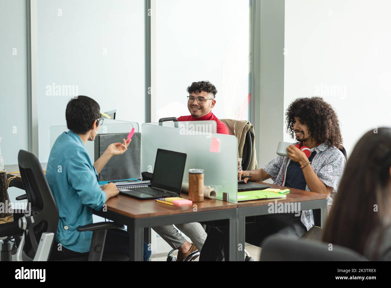 Group of positive Hispanic coworkers sitting at table with laptops and ...