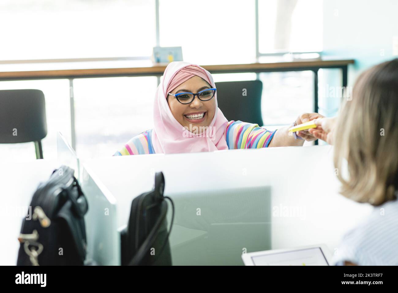 Positive Muslim female in hijab sitting at table and giving paper ...