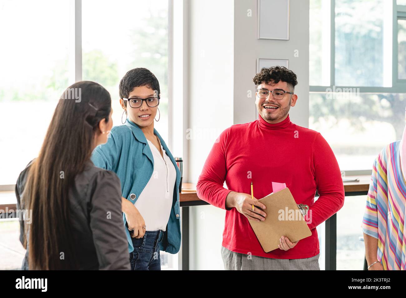 Positive Hispanic coworkers in casual clothes standing and talking with ...