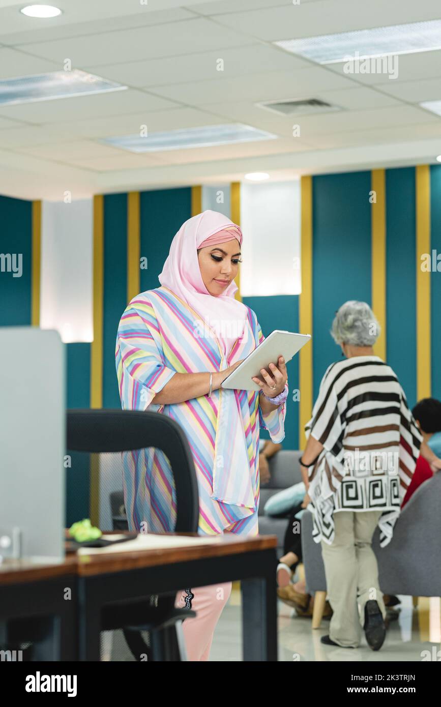 Muslim woman in pink hijab and colorful dress standing with tablet ...