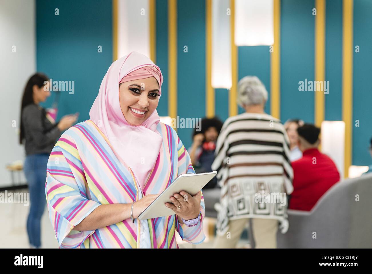 Positive Muslim woman in pink hijab and colorful dress standing with ...