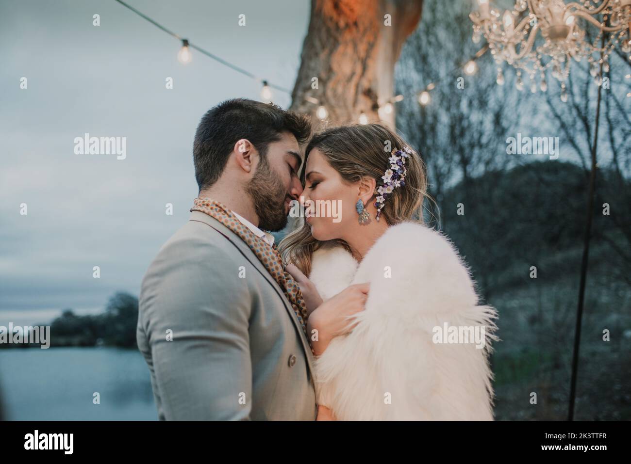 Young guy in suit kissing and embracing slim lady in wedding dress near ...