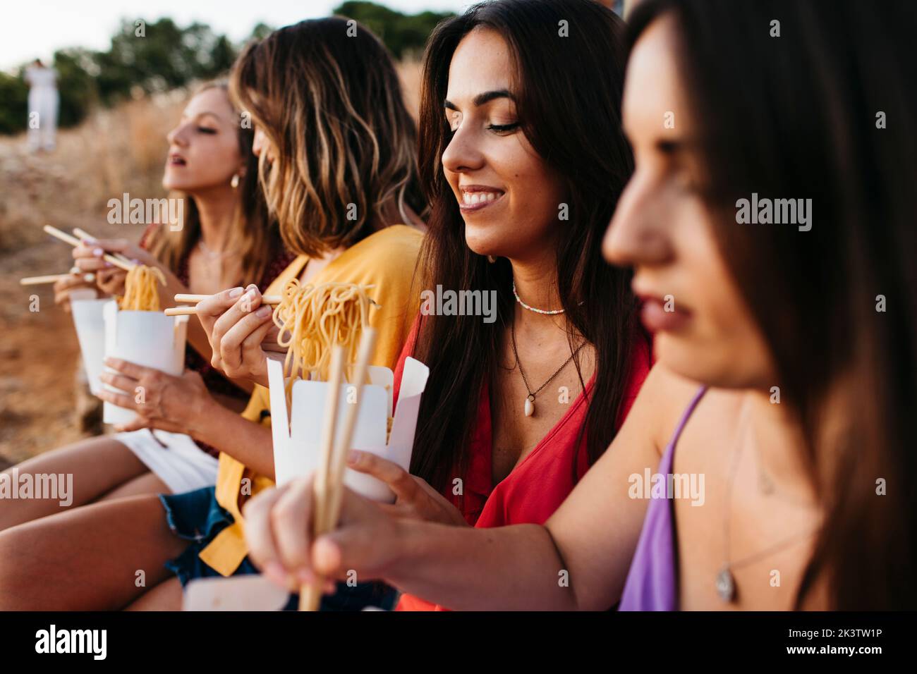 Cheerful female friends sitting with crossed legs on stone border while ...