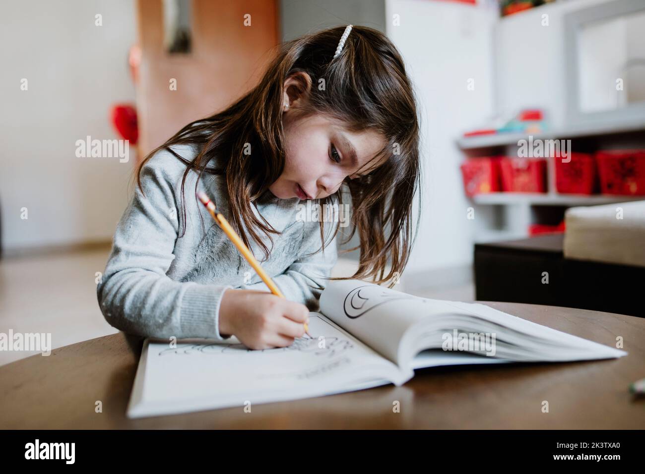 Focused girl drawing with pencil in album while sitting at wooden table ...