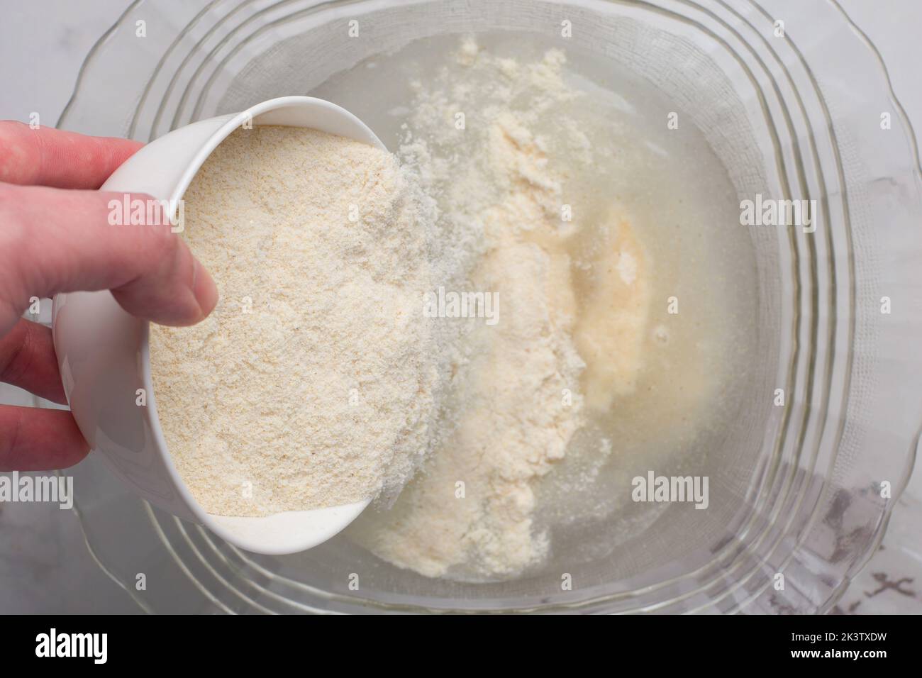 From above of faceless housewife adding flour to mix dough in glass ...