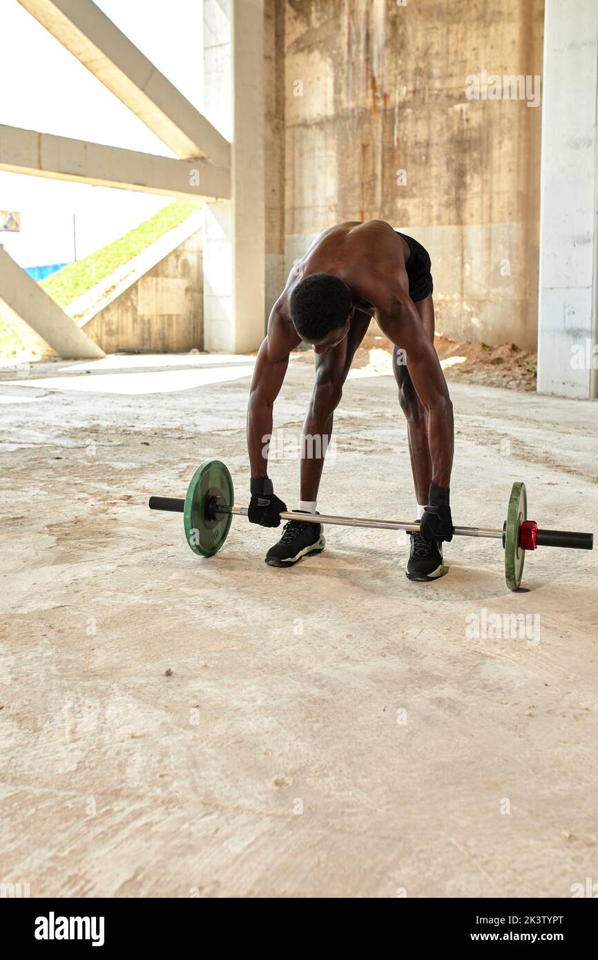Athletic black young man lifting a heavy-weight barbell in outdoor gym ...