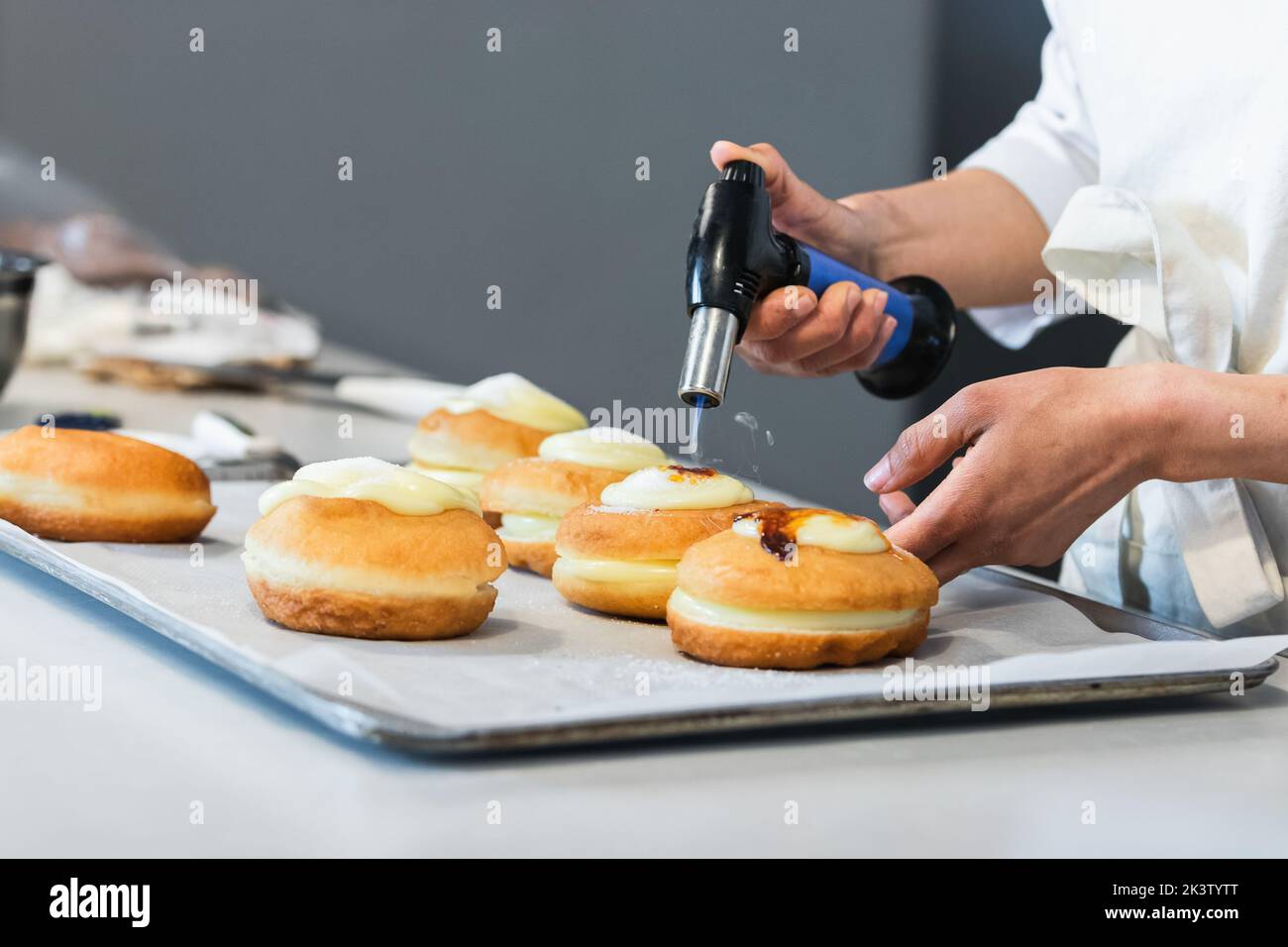 Unrecognizable crop chef caramelizing sugar cream on sweet Berliners ...