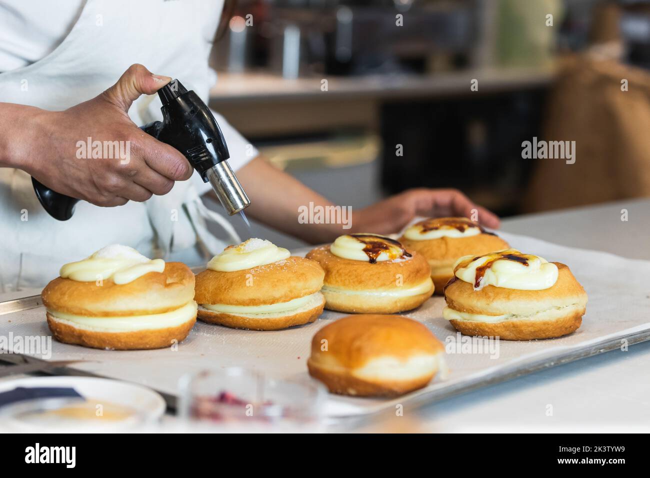 Unrecognizable crop chef caramelizing sugar cream on sweet Berliners ...