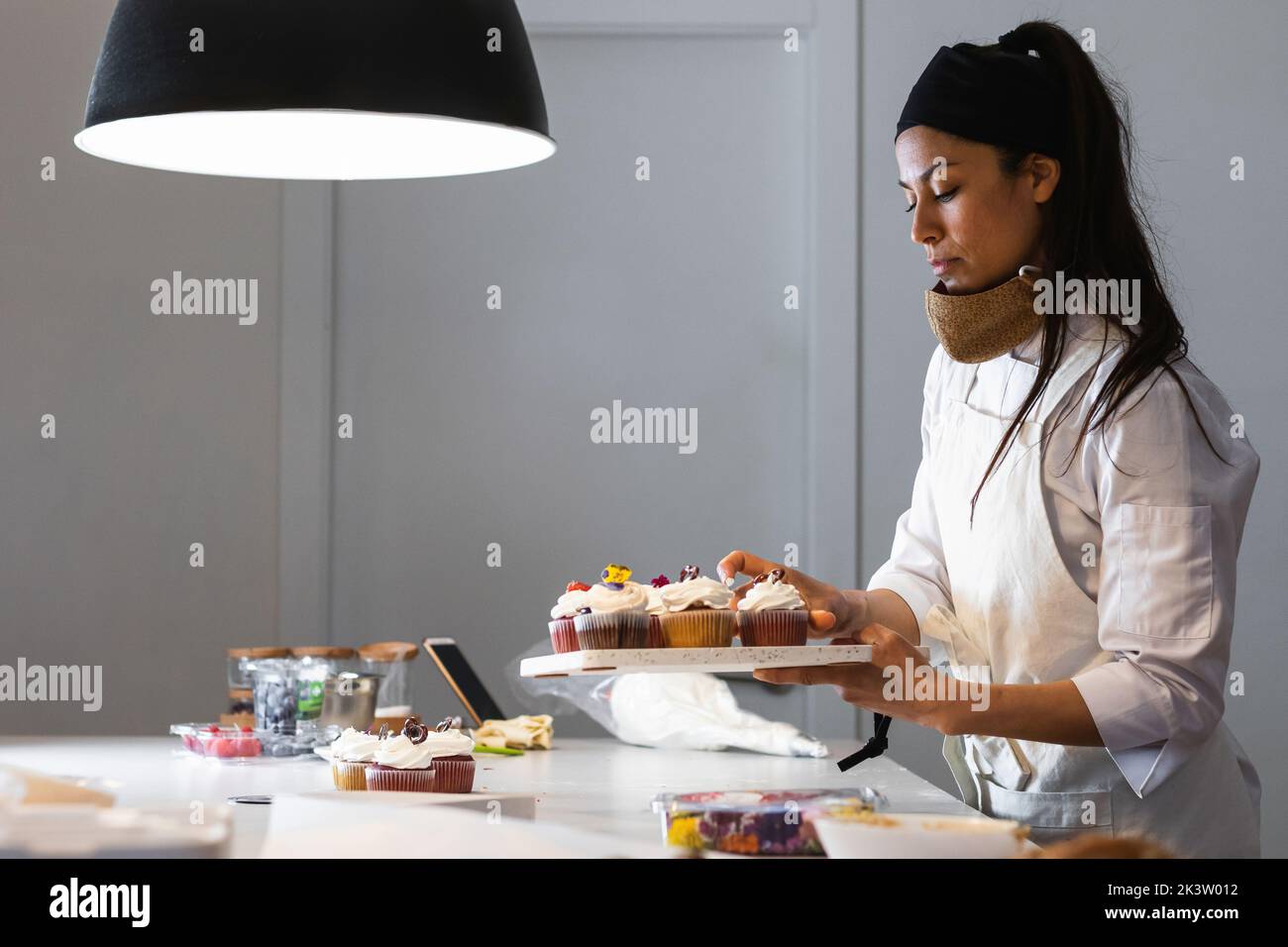 Side view of female baker in uniform standing at table in bakery with ...
