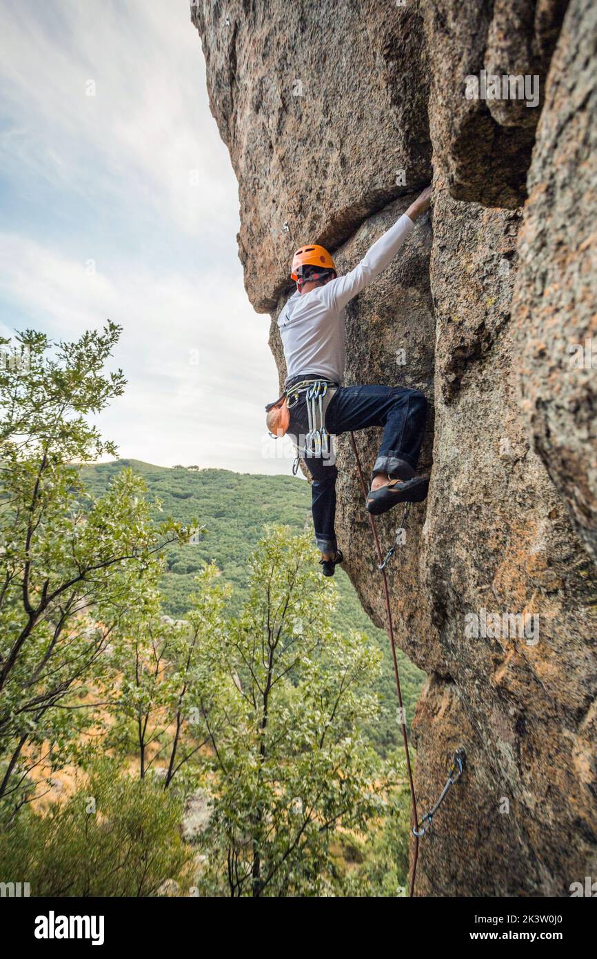 Male mountaineer climbing high cliff with safety carabiner and ropes ...