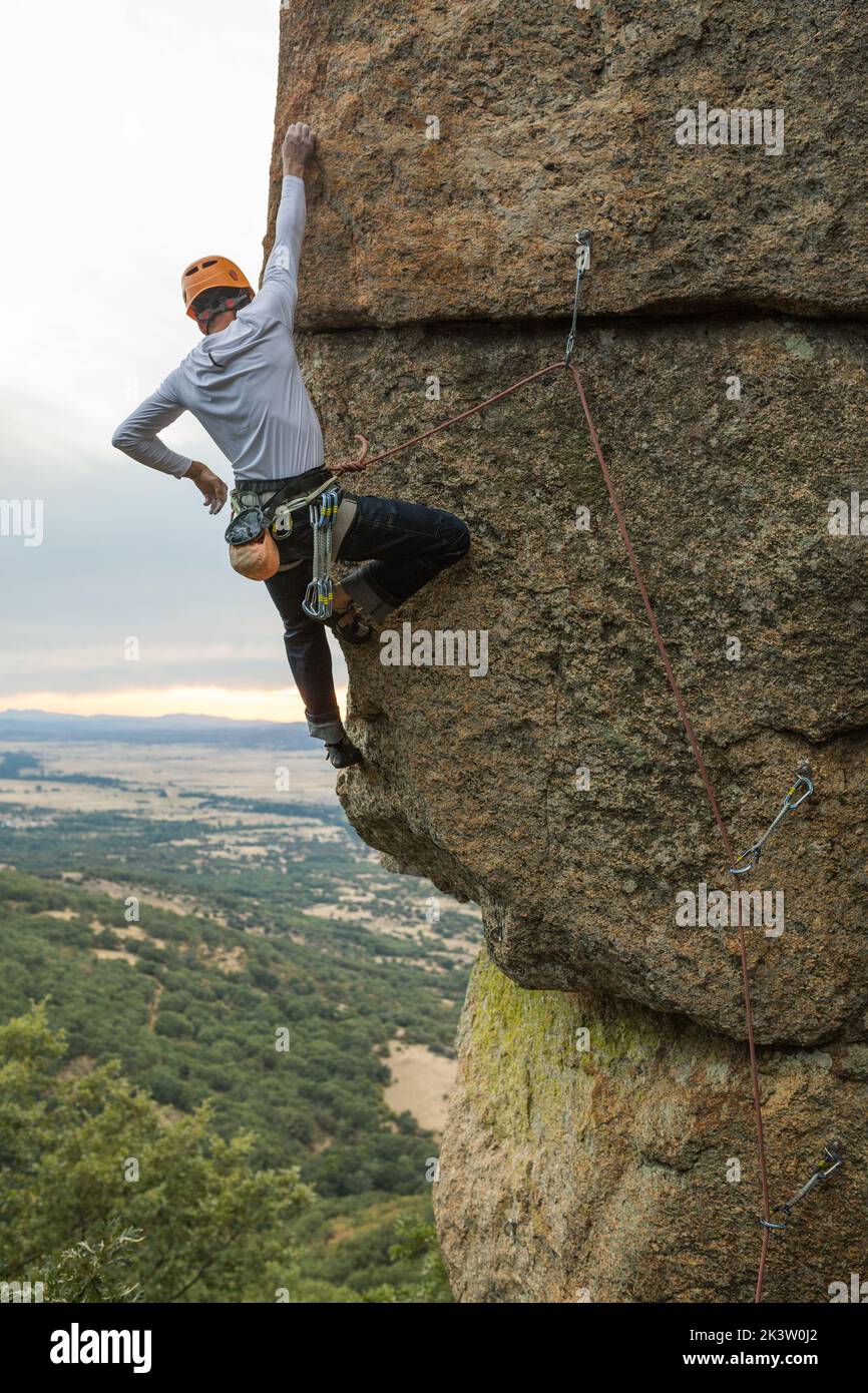 Male mountaineer climbing high cliff with safety carabiner and ropes ...