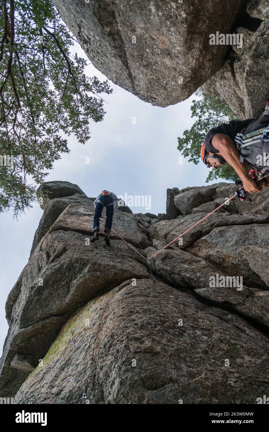 From below climber in helmet holding rope and insuring partner crawling ...