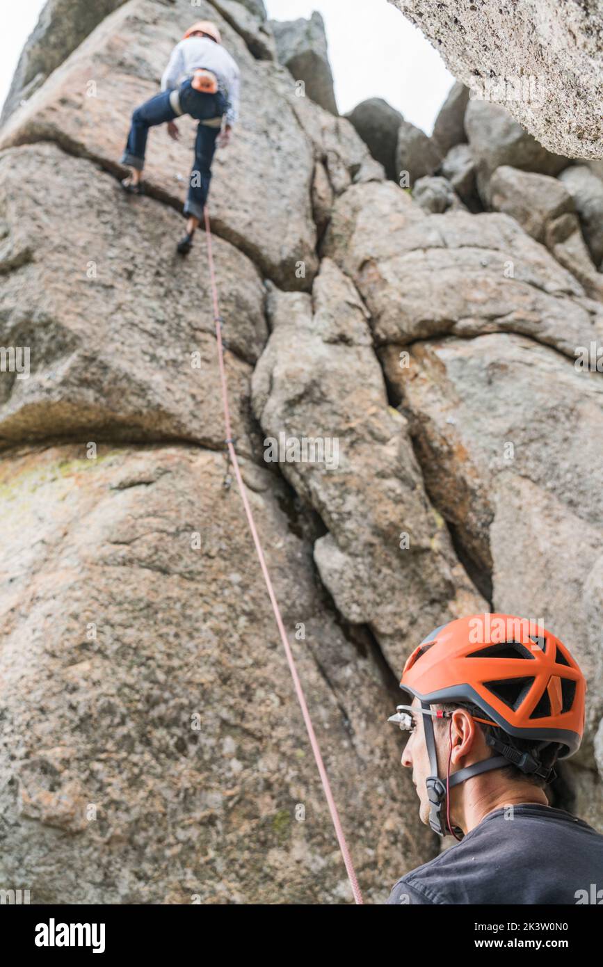 From below climber in helmet holding rope and insuring partner crawling ...