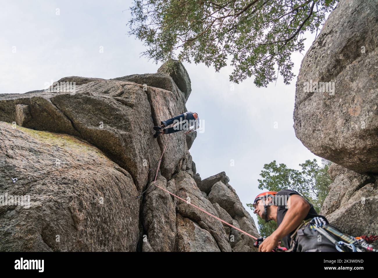 From below climber in helmet holding rope and insuring partner crawling ...