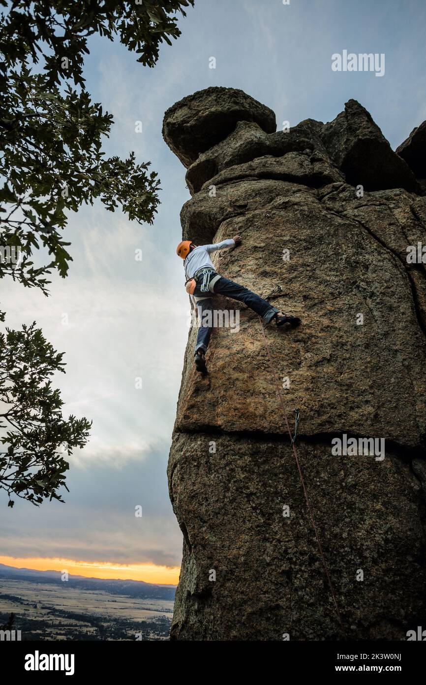 Male mountaineer climbing high cliff with safety carabiner and ropes ...