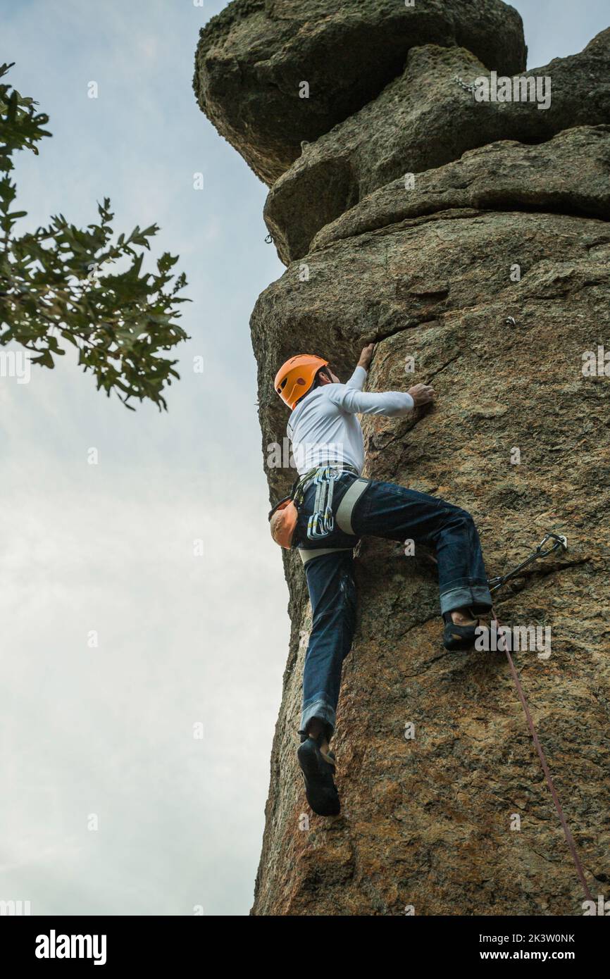 Male mountaineer climbing high cliff with safety carabiner and ropes ...