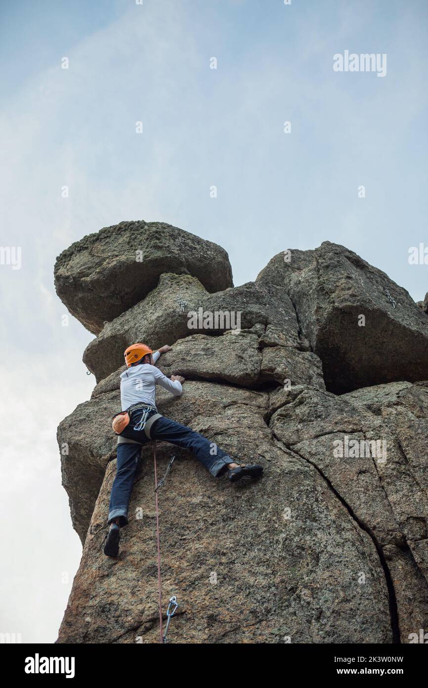 Male mountaineer climbing high cliff with safety carabiner and ropes ...
