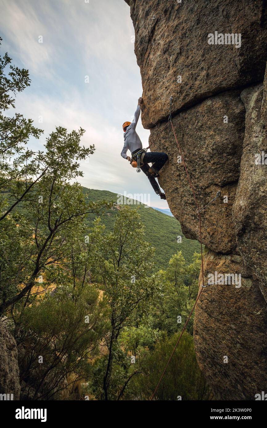 Male mountaineer climbing high cliff with safety carabiner and ropes ...